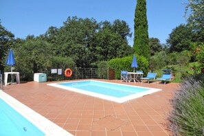 Piscina retangular com deck ladrilhado, cercada por vegetação e árvores.