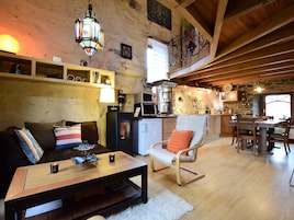Um interior rústico com uma mesa de jantar de madeira, um sofá com almofadas listradas, uma mesa de centro e uma cozinha com micro-ondas e fogão.
