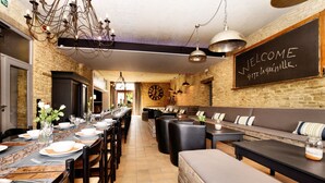 Um restaurante com uma mesa de jantar comprida, várias cadeiras, área de bar e um espaço de estar com um letreiro que diz 'Welcome'.