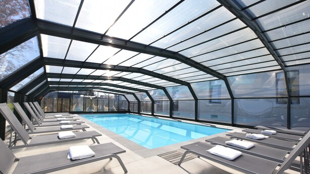 Piscina coberta com espreguiçadeiras e teto de vidro.