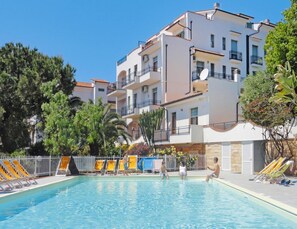 Piscina com espreguiçadeiras e um edifício com varandas ao fundo.