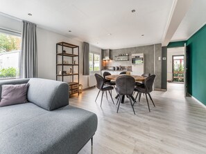 Uma sala de estar moderna com um sofá cinzento, uma mesa de jantar de madeira com seis cadeiras e uma estante embutida.
