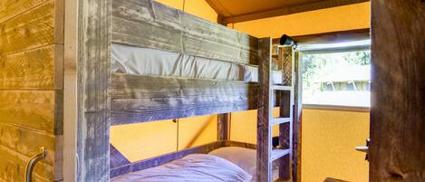 Uma cama beliche com escada, paredes de madeira e janela com vista para árvores.