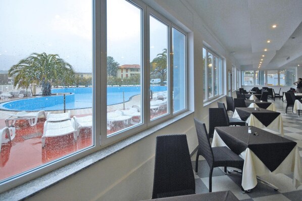 Restaurante com grandes janelas voltadas para uma área de piscina.
