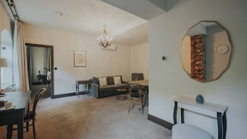 Uma sala de estar com um sofá, cadeiras, uma mesa de jantar, um lustre e um espelho na parede.