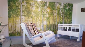 Quarto com uma cadeira de balanço branca, um berço branco e um mural na parede com tema de floresta.