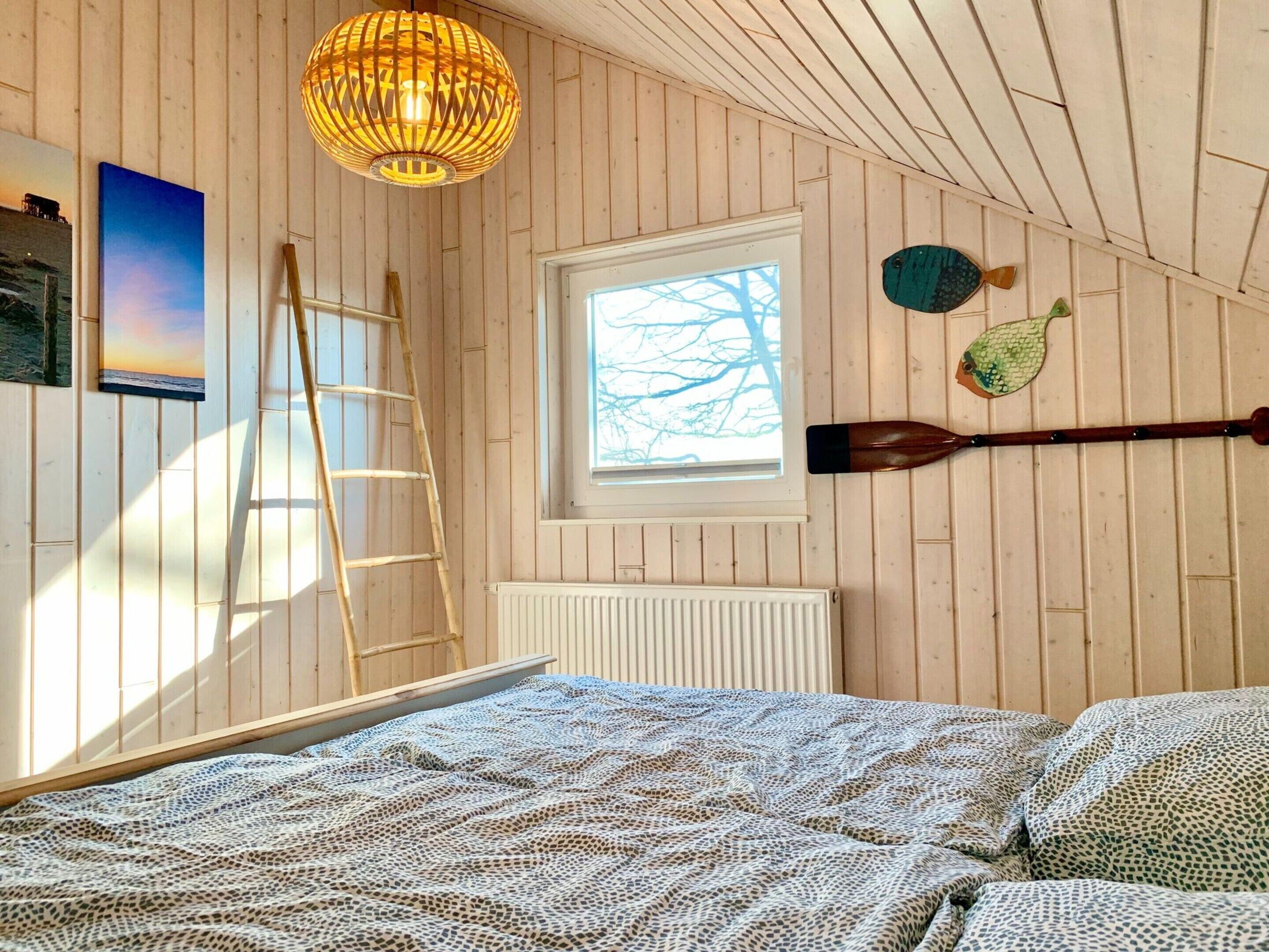 Um quarto revestido em madeira, com uma cama, uma escada, uma janela e um remo de surf fixado na parede.