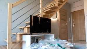 Quarto moderno com escada de madeira, TV de tela plana sobre um suporte branco e um saco plástico no chão.