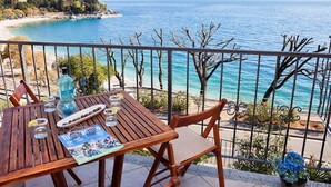 Mesa de madeira com cadeiras numa varanda com vista para a praia e o mar.