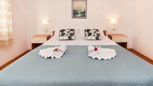 Quarto de hotel com uma cama grande, duas mesas de cabeceira, um quadro na parede e uma janela com cortinas.