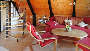 Quarto aconchegante com escada de madeira, sofá vermelho e mesa de jantar de madeira.