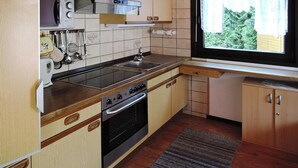 Uma cozinha compacta com armários de madeira, micro-ondas embutido, fogão e janela com vista para o verde.