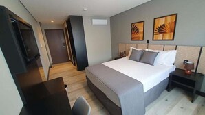 Quarto de hotel com cama, mesas de cabeceira, escrivaninha e obras de arte nas paredes.