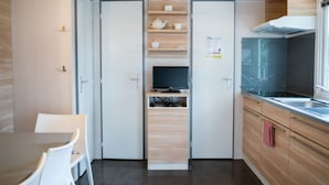 Uma cozinha compacta com TV integrada, armários de madeira e um espaço de refeições com cadeiras brancas.