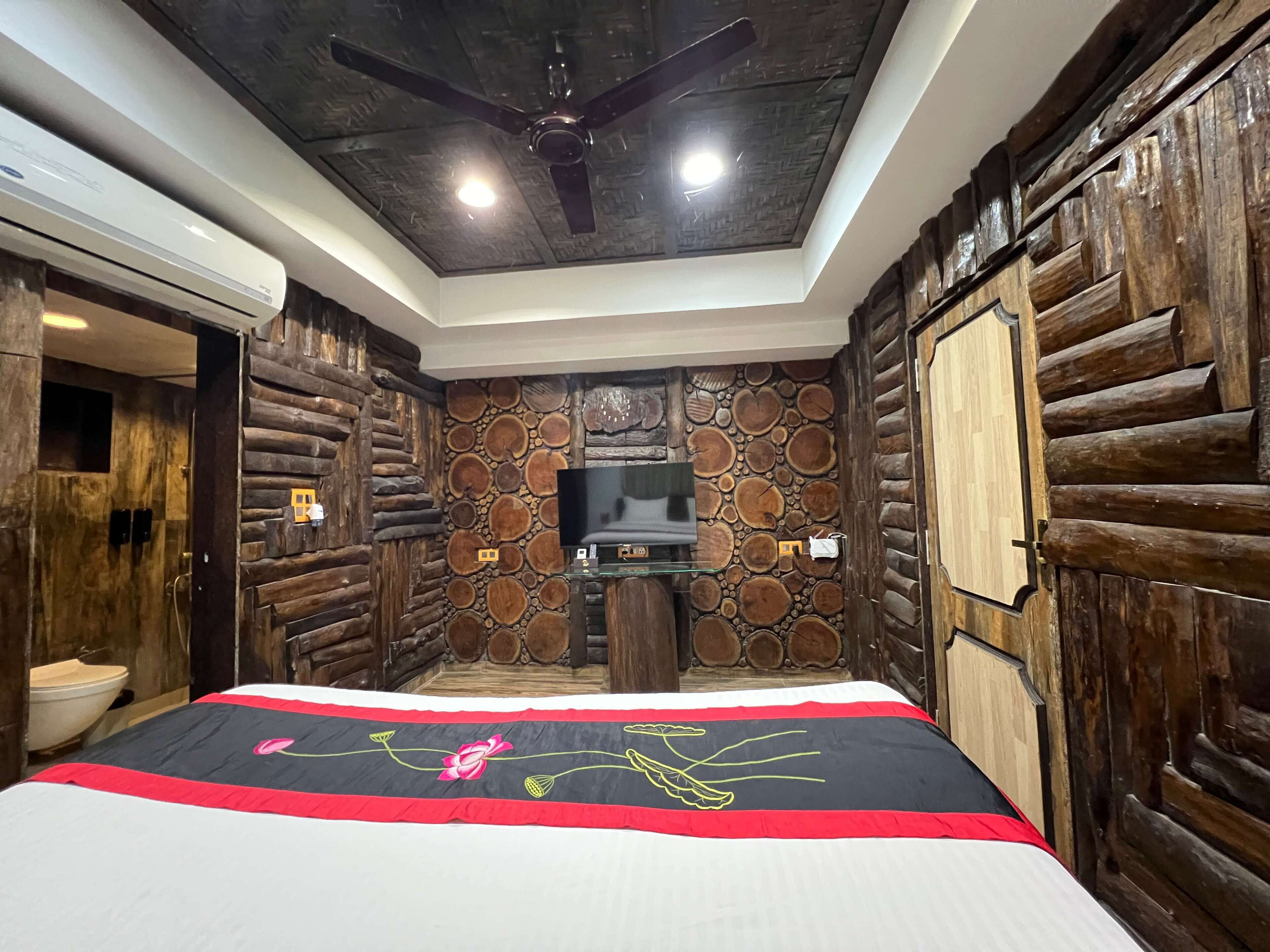 Quarto com cama, ventoinha no teto, televisão e paredes de madeira.