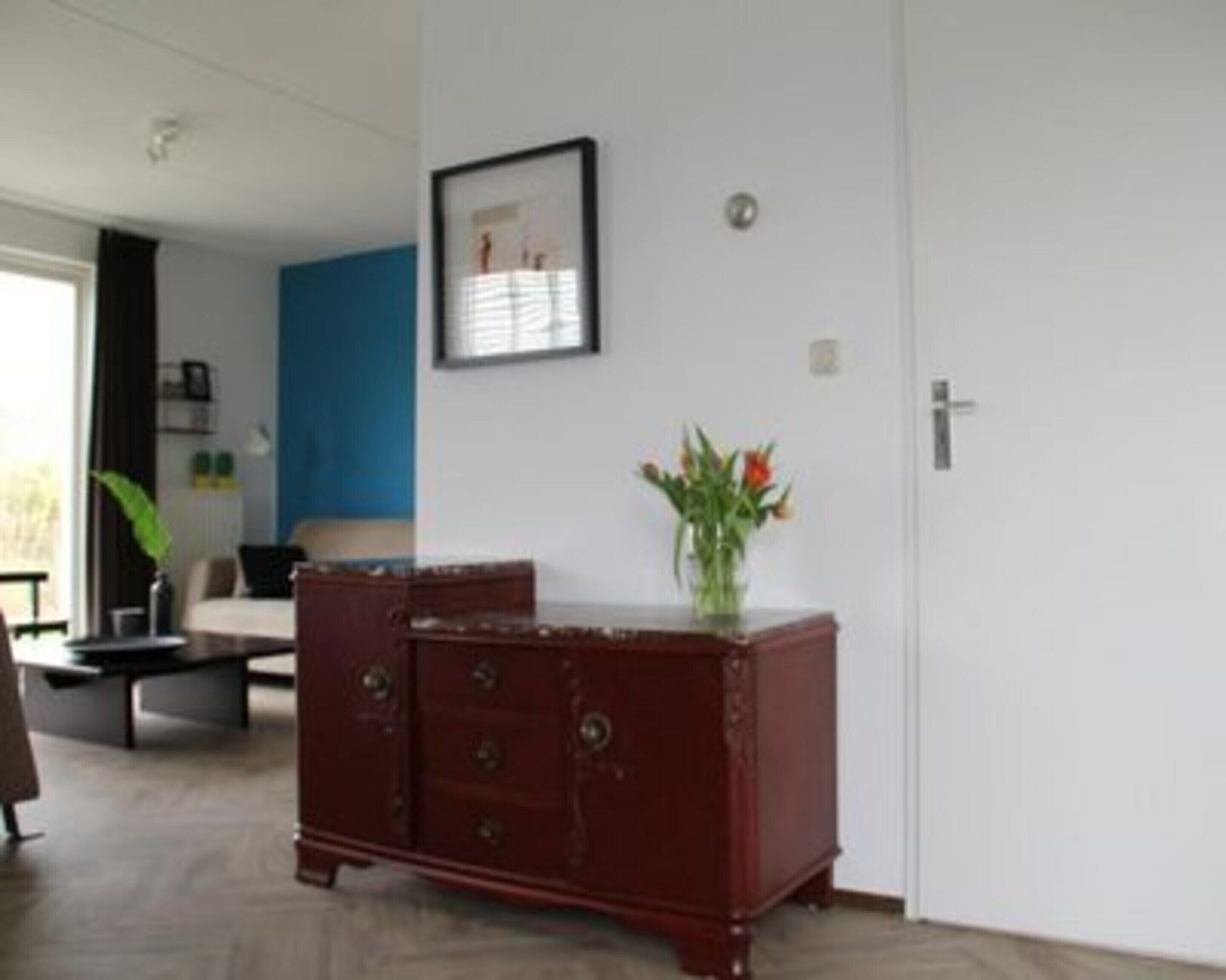 Uma sala de estar com um armário de madeira escura, um quadro pendurado na parede e um vaso com flores sobre uma mesa.
