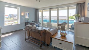 Quarto de hotel moderno com área de refeições, uma janela grande com vista para uma piscina e uma varanda com espaço para sentar ao ar livre.