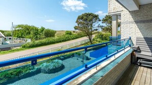 Piscina com deck azul, um edifício branco com fachada de pedra e uma estrada com cerca branca ao fundo.