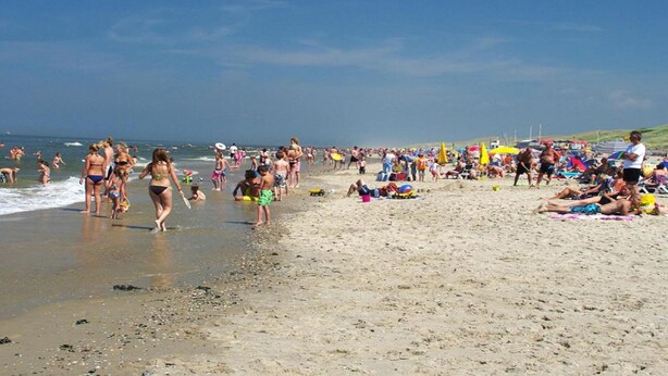 Uma praia cheia de gente caminhando e relaxando.