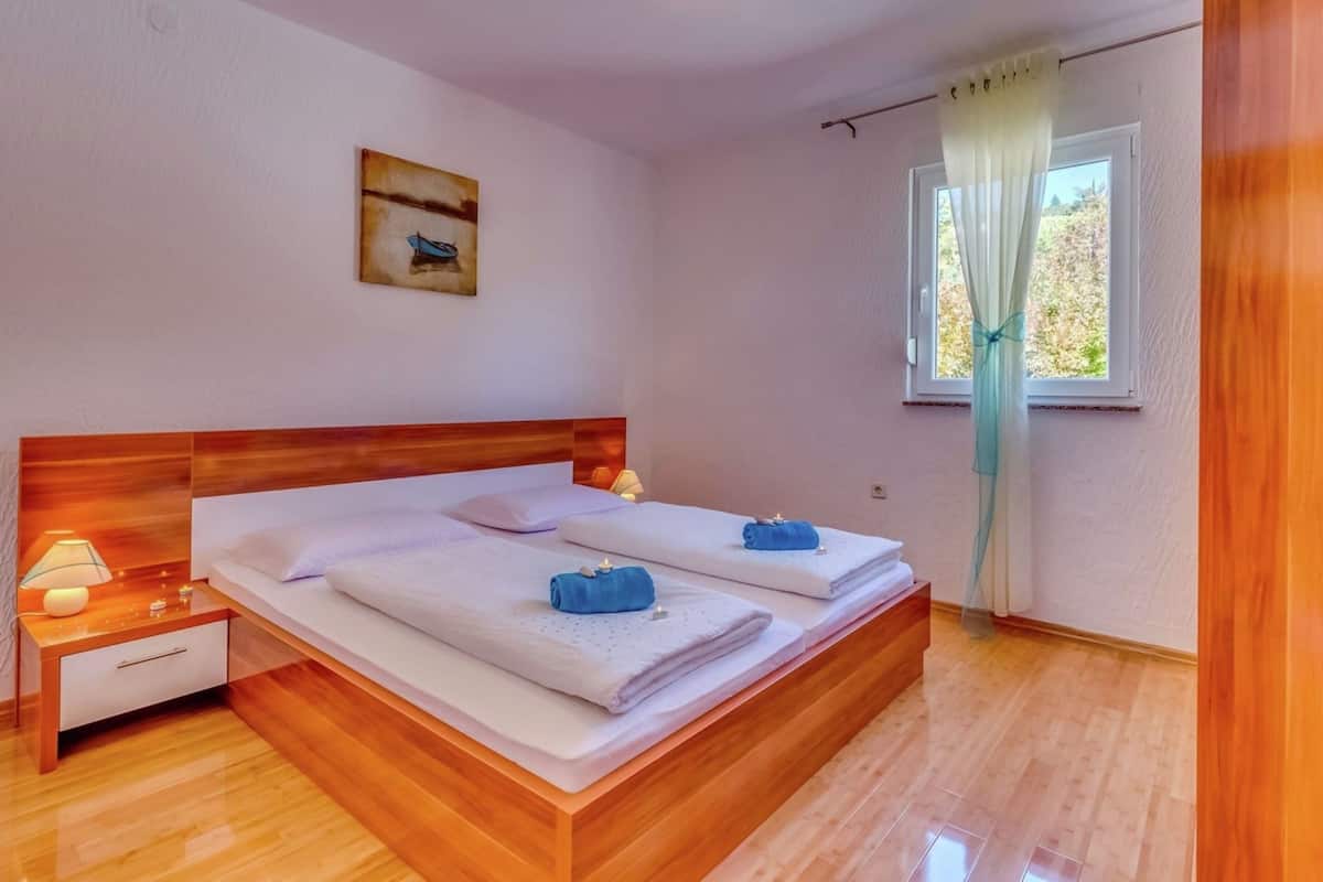 Uma cama de casal com cabeceira de madeira, uma mesa de cabeceira com abajur e uma janela com cortinas.