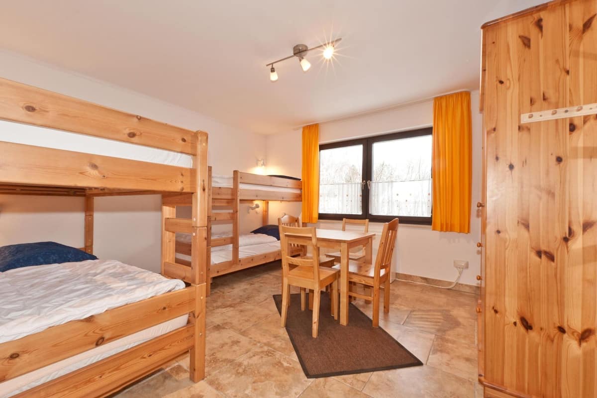Quarto com beliche, mesa de madeira e cadeiras, janela com cortinas e guarda-roupa de madeira.