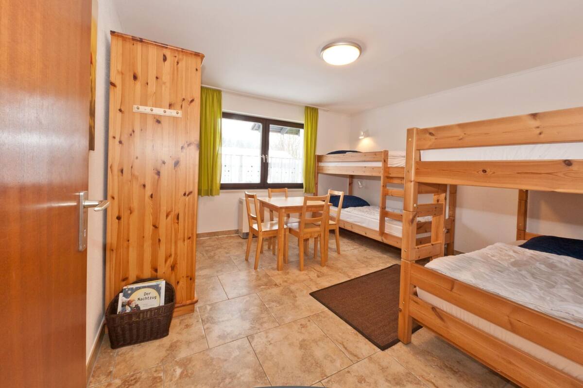 Um quarto pequeno e acolhedor com beliches, um guarda-roupa de madeira, uma mesa de jantar com cadeiras e uma janela com cortinas.