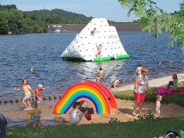 Um parque aquático com um grande escorregador inflável, uma estrutura de recreação em arco-íris e um lago com barcos ao fundo.