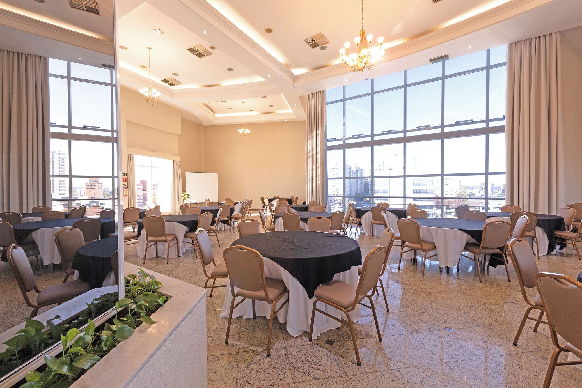 Sala de conferências com várias mesas, cadeiras, amplas janelas e um quadro branco.