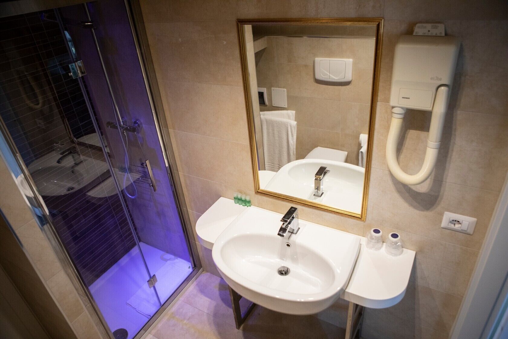 Casa de banho moderna com chuveiro envidraçado, lavatório branco com espelho e chuveiro de mão.