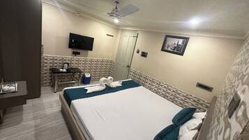 Quarto de hotel com uma cama, uma mesa, uma cadeira, uma televisão e um quadro na parede.
