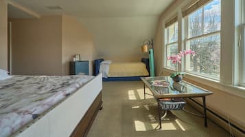 Quarto com cama, escrivaninha, cadeira, janela com persianas e vista para árvores.