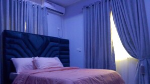 Quarto com cama, cabeceira e cortinas.