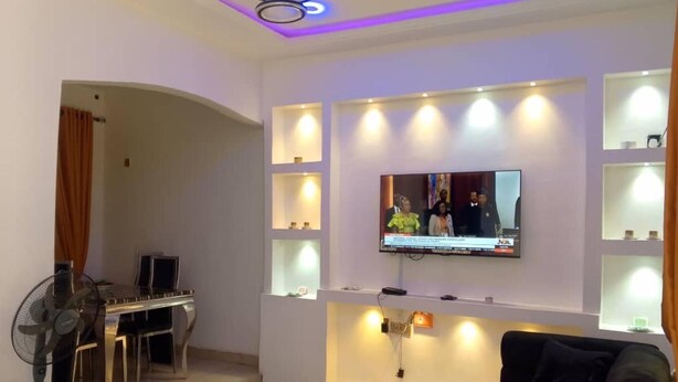 Uma sala de estar moderna com uma TV de tela plana na parede, um sofá, uma mesa de centro e um espaço de jantar com mesa e cadeiras.