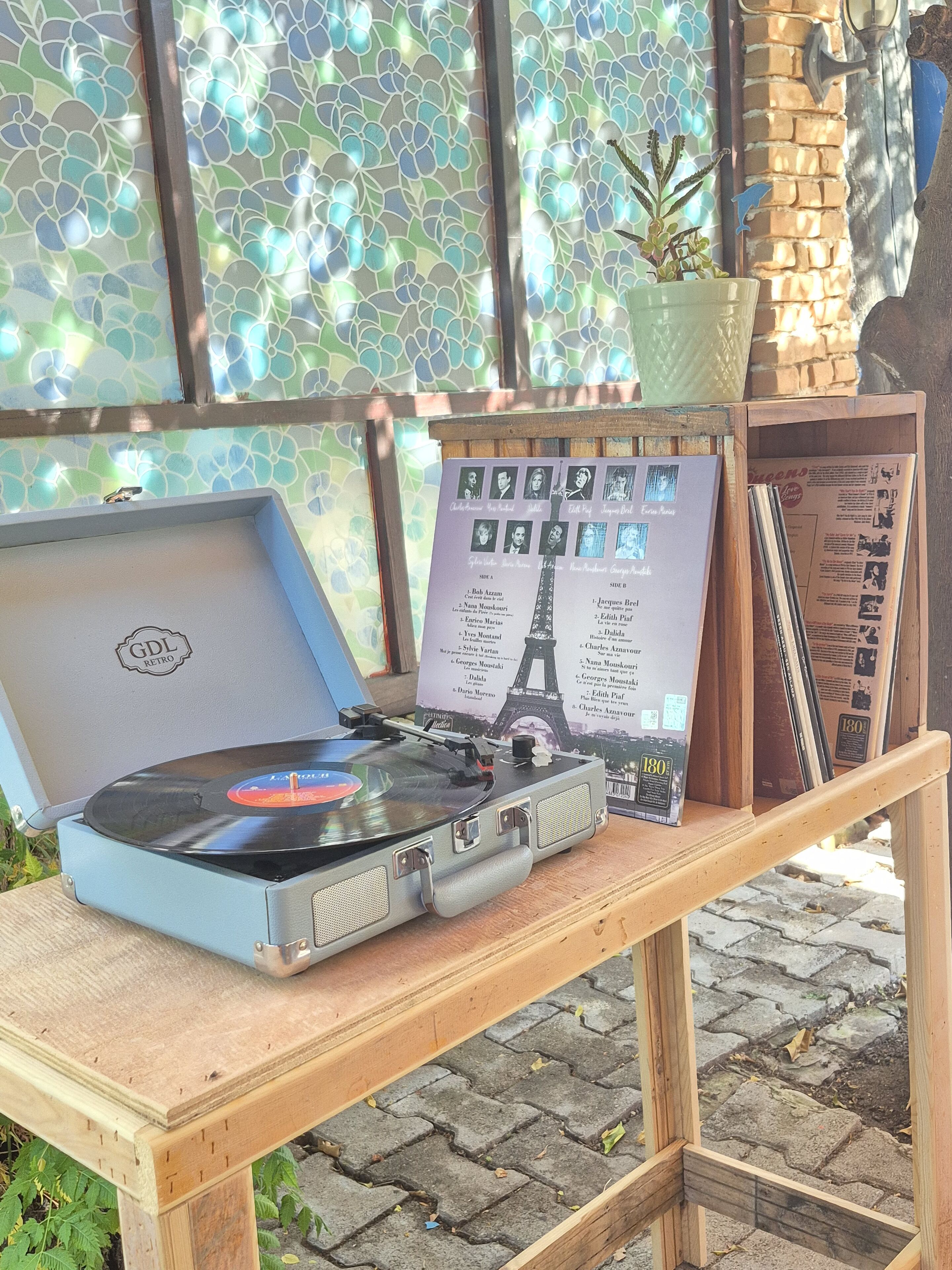 Um toca-discos sobre uma mesa de madeira com um cartaz da Torre Eiffel e uma planta.