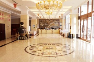 Um hall de hotel com balcão de recepção, um lustre e uma janela grande.