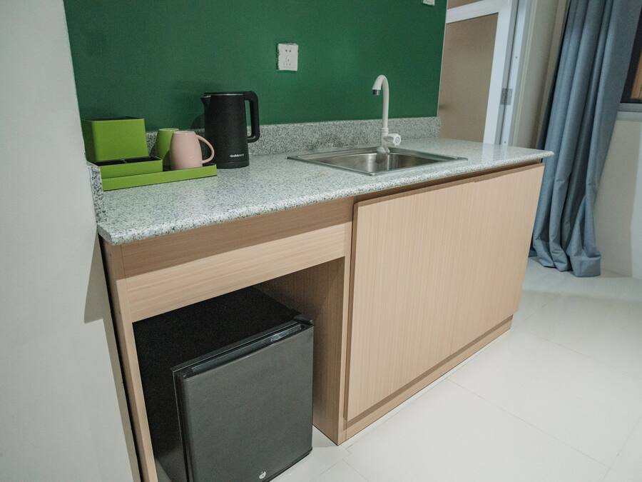 Uma cozinha compacta com pia embutida, uma pequena geladeira e uma cafeteira na bancada.