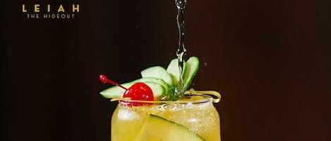 Um cocktail com uma fatia de pepino e uma cereja na borda, sendo servido num copo.