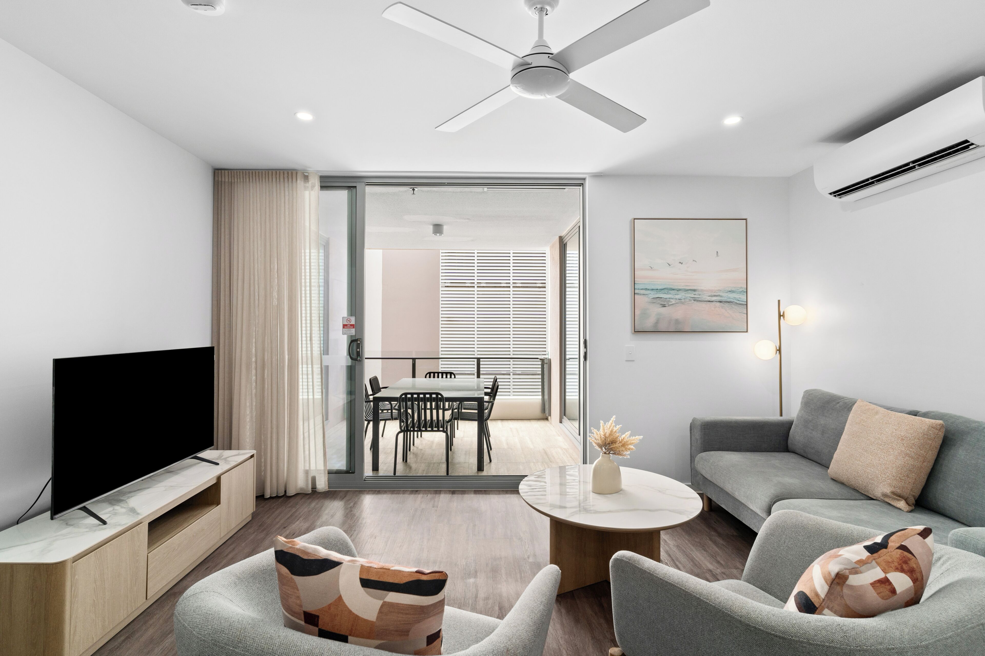 Uma sala de estar moderna com televisão de tela plana, sofás cinzas, uma mesa de centro e um ventilador de teto.