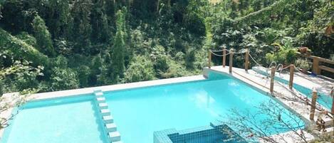 Piscina retangular com degraus para acesso, rodeada por vegetação exuberante e árvores.