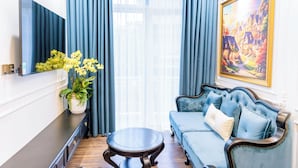 Uma sala de estar com um sofá azul, uma mesa de centro redonda, uma TV fixada na parede e um quadro acima do sofá.