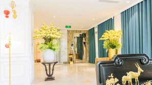 Um hall de hotel com piso de mármore, uma mesa de recepção, um sofá decorado com um cervo e duas plantas em vasos com flores amarelas.
