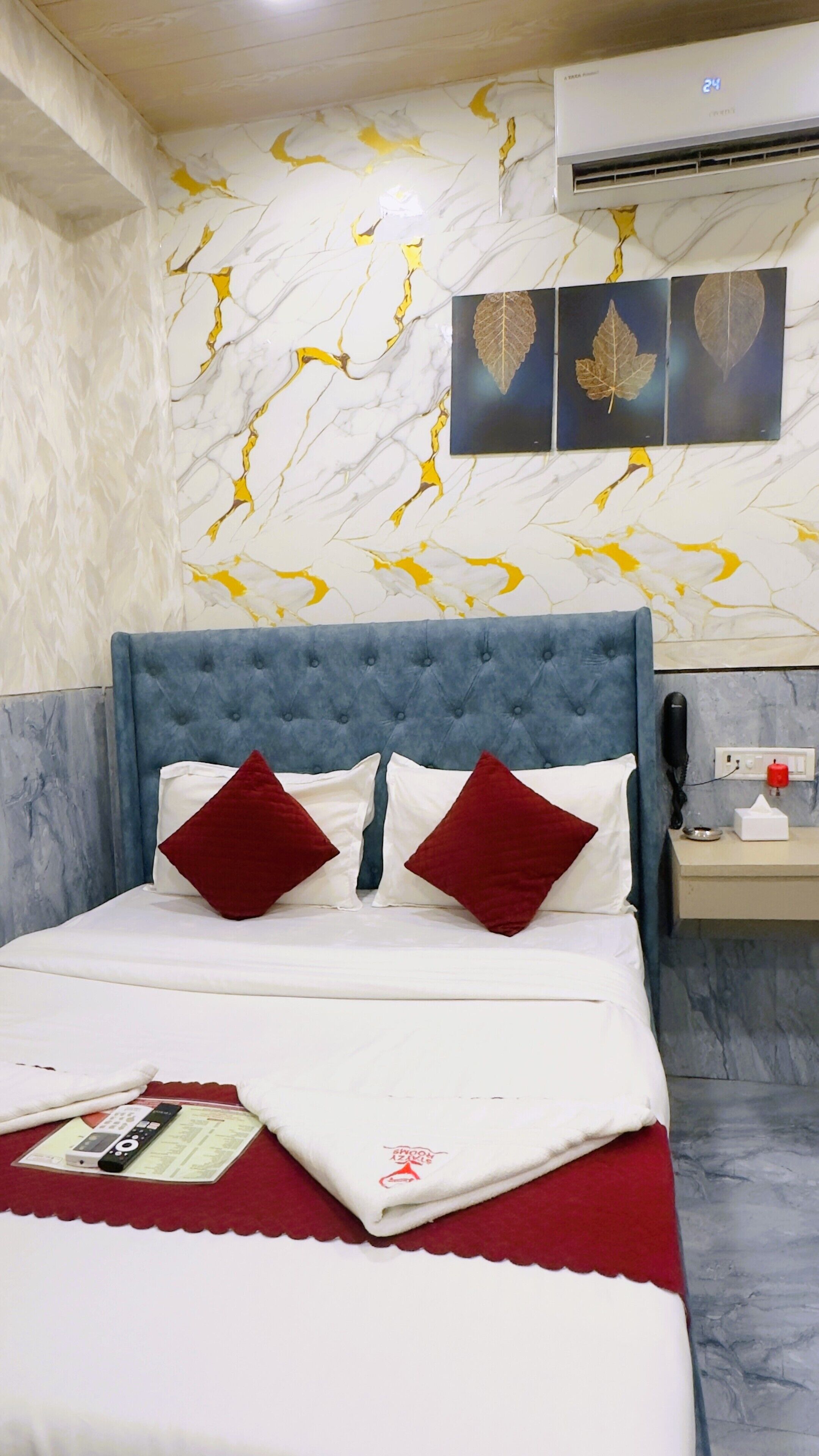 Quarto de hotel com parede estampada em mármore, cabeceira azul com detalhes em botão e mesa de cabeceira com telefone e caixa de lenços.