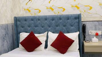 Quarto de hotel com parede estampada em mármore, cabeceira azul com detalhes em botão e mesa de cabeceira com telefone e caixa de lenços.