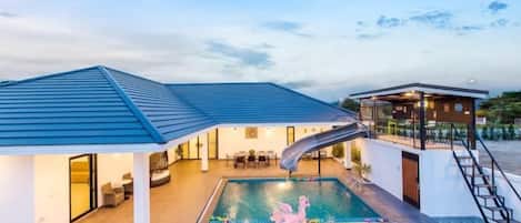 Uma casa moderna com piscina, um alpendre coberto e um pequeno edifício com estrutura de vidro.