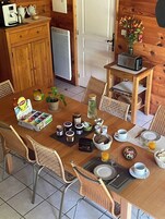 Uma área de refeições de madeira com uma mesa posta para o café da manhã, incluindo pão, manteiga, geleia e uma cafeteira.