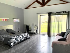 Quarto moderno com uma cama grande, uma escrivaninha e um sofá. Há uma porta de vidro deslizante que dá para uma varanda.