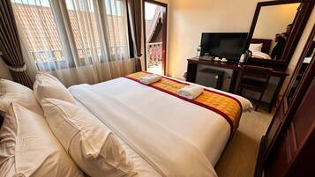 Quarto de hotel com uma cama grande, televisão, escrivaninha com cadeira e janela com cortinas.