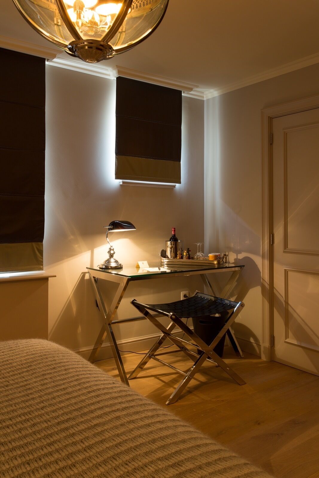 Quarto compacto com uma cadeira dobrável, uma escrivaninha com uma luminária e uma garrafa sobre ela.