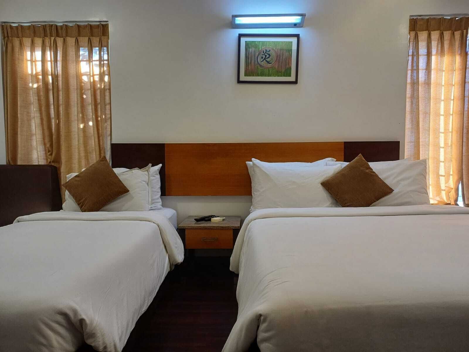 Quarto de hotel com duas camas, uma cabeceira de madeira, uma mesinha de cabeceira e um quadro na parede.