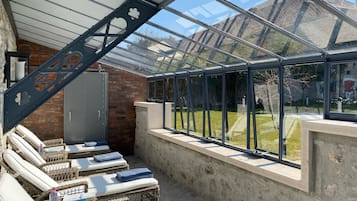Uma sala de sol com móveis de vime, vista para o jardim e escada de metal.